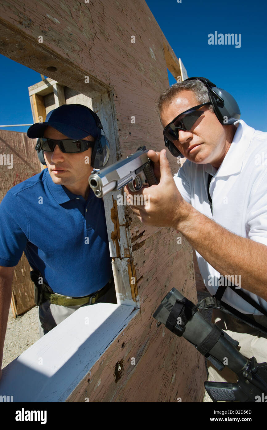 Instructor assisting man aiming hand gun at firing range Stock Photo ...