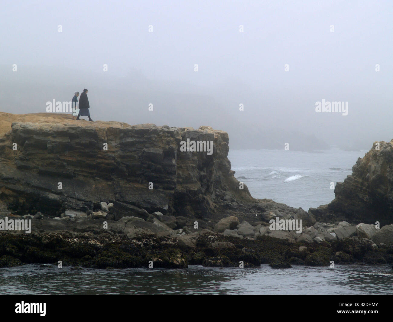 Two women walking hand in hand on rocky cliff on misty day along the ...