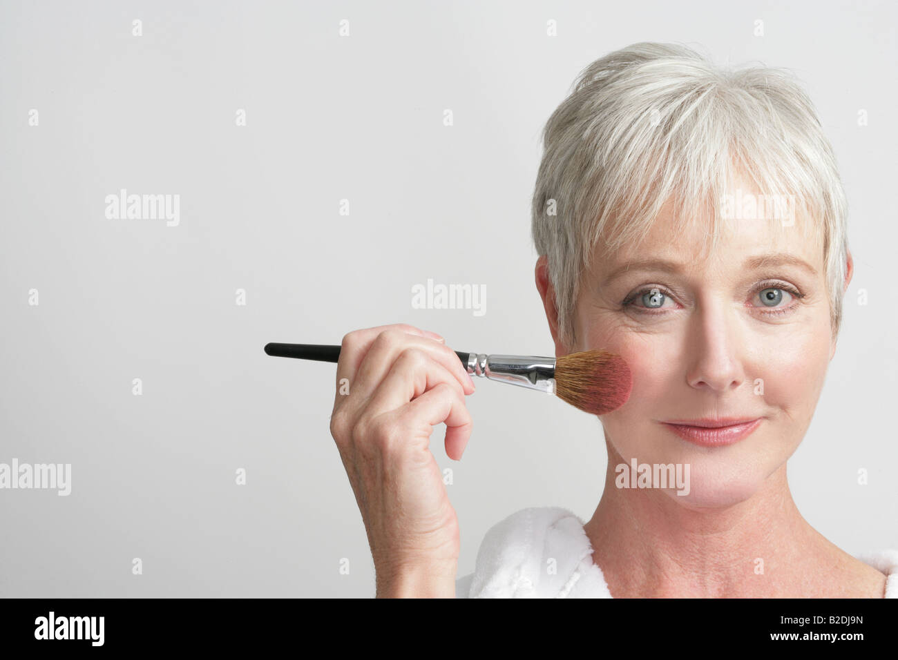 Mature woman using blush brush Stock Photo - Alamy