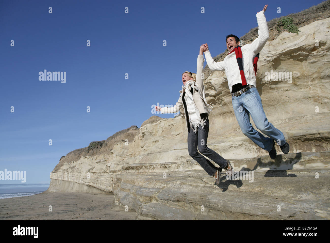 Young couple jumping off cliff at beach Stock Photo - Alamy