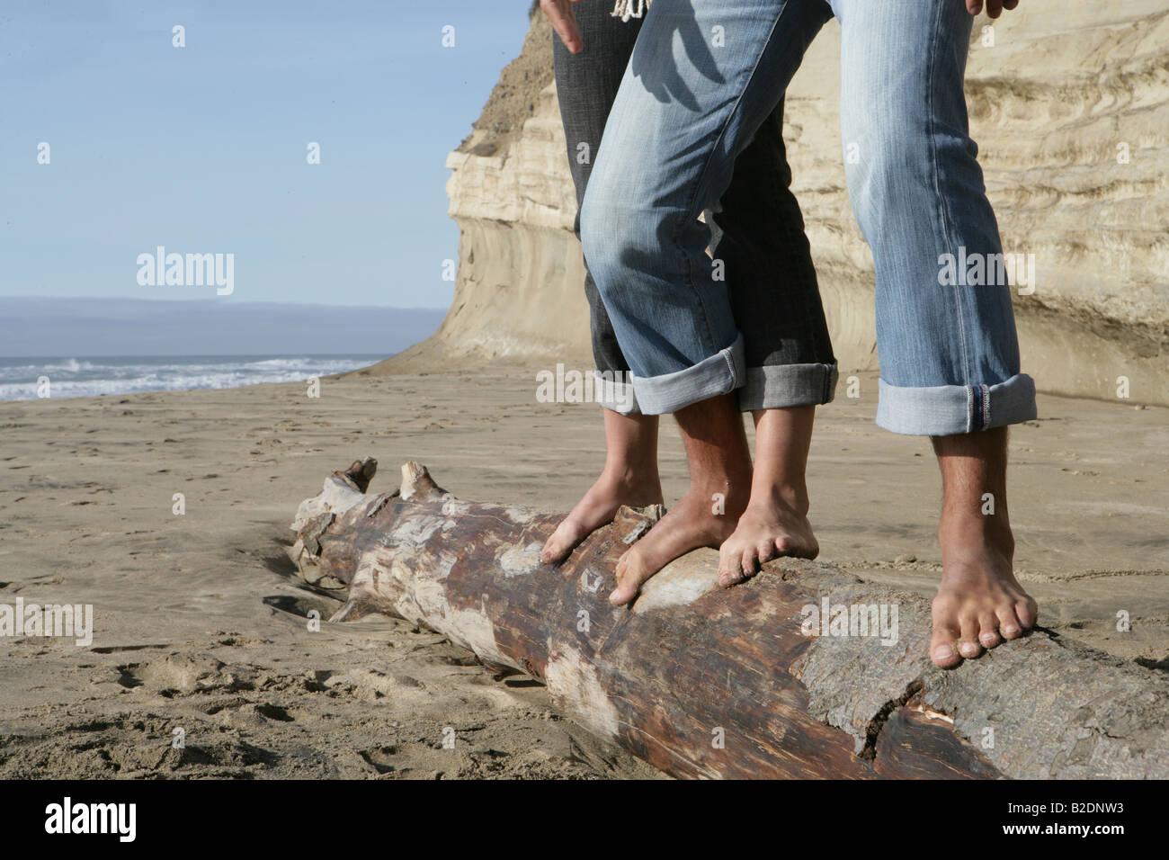 Cropped view of couple balancing on log at beach Stock Photo - Alamy