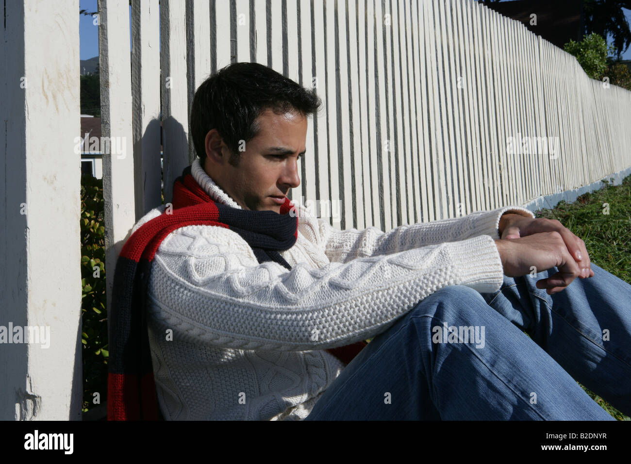 Young man sitting near fence Stock Photo - Alamy