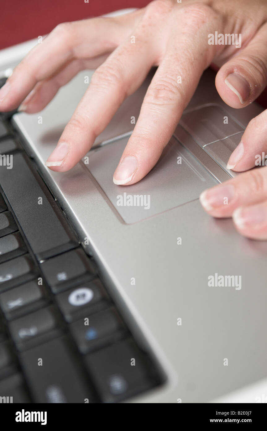 Detail view of a woman's hands using a laptop keyboard and track pad ...