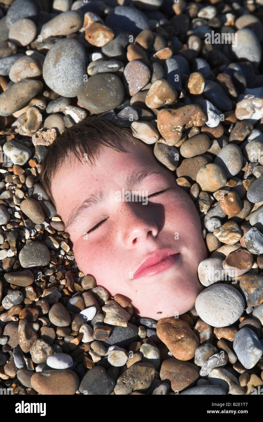Boy's face buried in shingle beach Stock Photo - Alamy