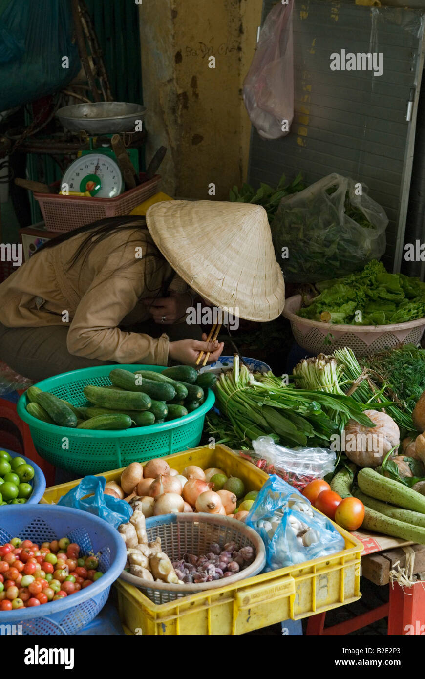 A Vietnamese vegetable shop owner wearing a conical leaf hat enjoys ...