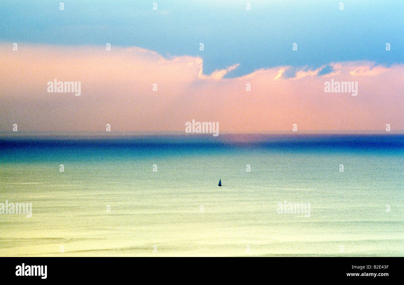 Lone yacht sailing across calm open sea ocean in evening morning light ...