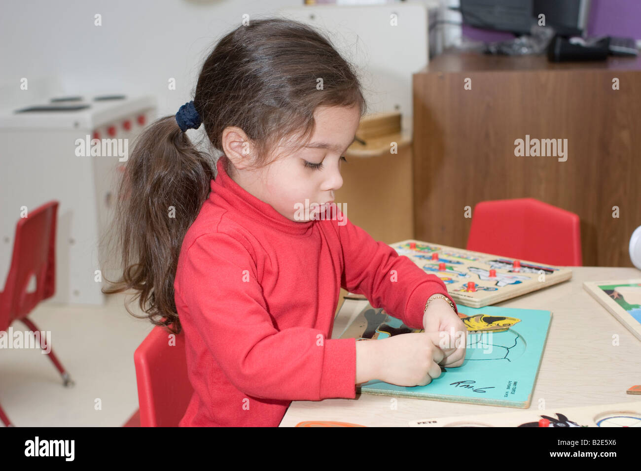 4 year old pre school girl sitting at a table doing a puzzle Stock ...
