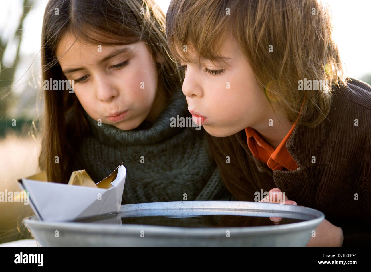 Close-up of two children blowing the paper boat on a bowl of water ...