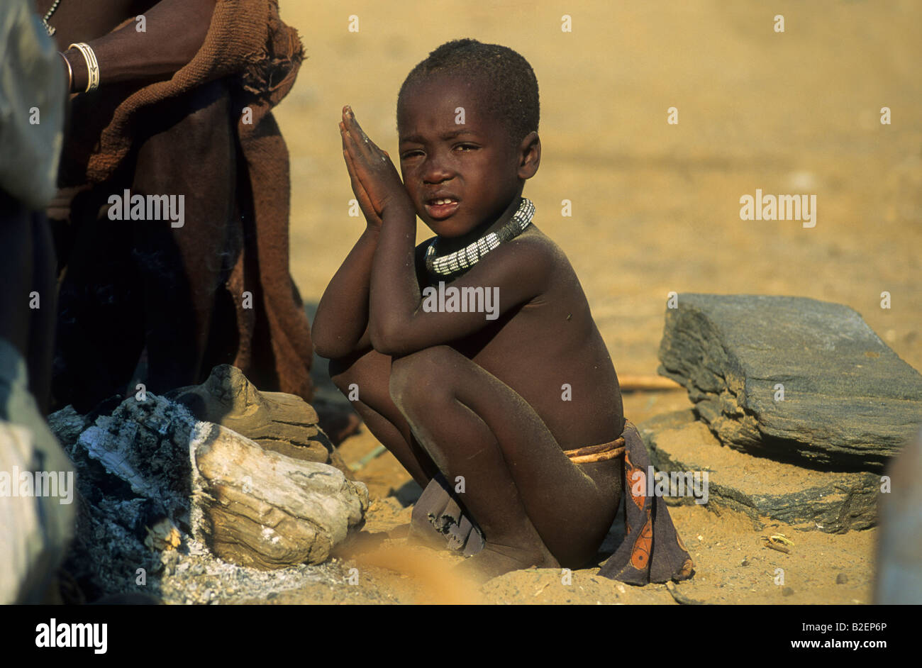 A Himba child sitting on its haunches next to a fire Stock Photo - Alamy