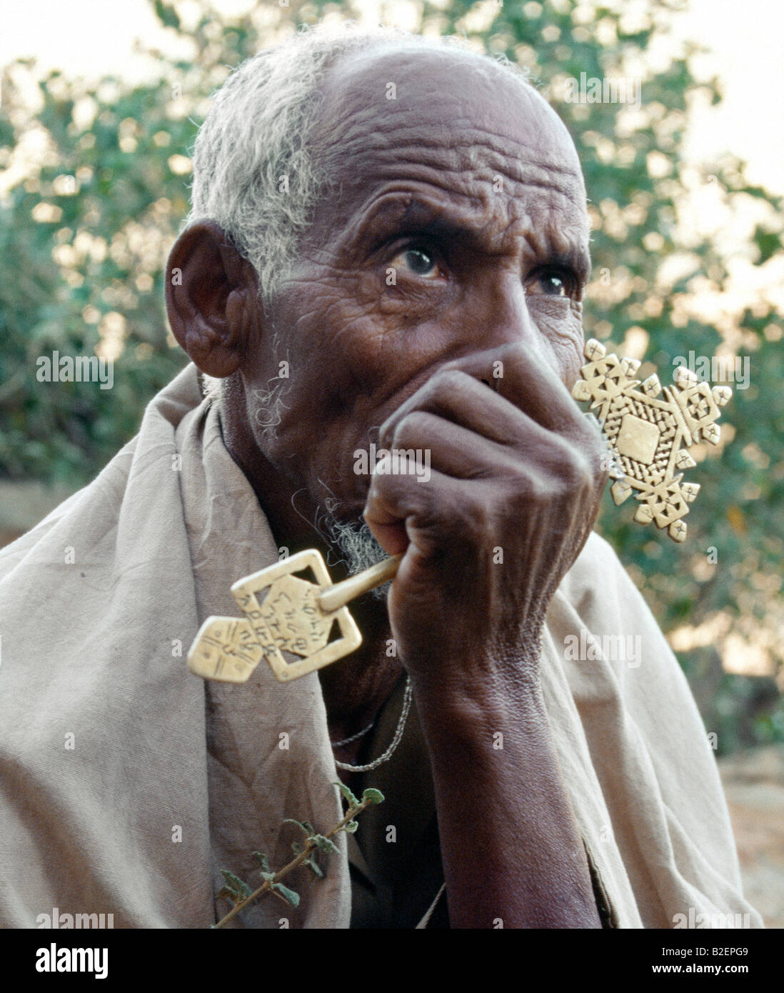 Deep in thought, an old man with Orthodox cross in hand rests outside ...