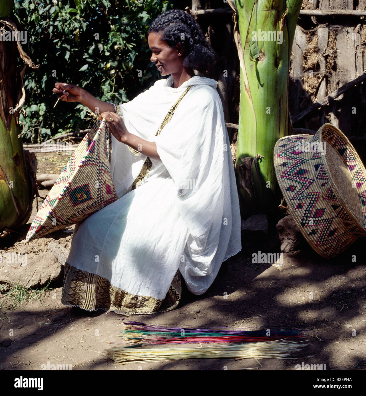 A young Amhara lady weaves a traditional food basket from dried grasses ...