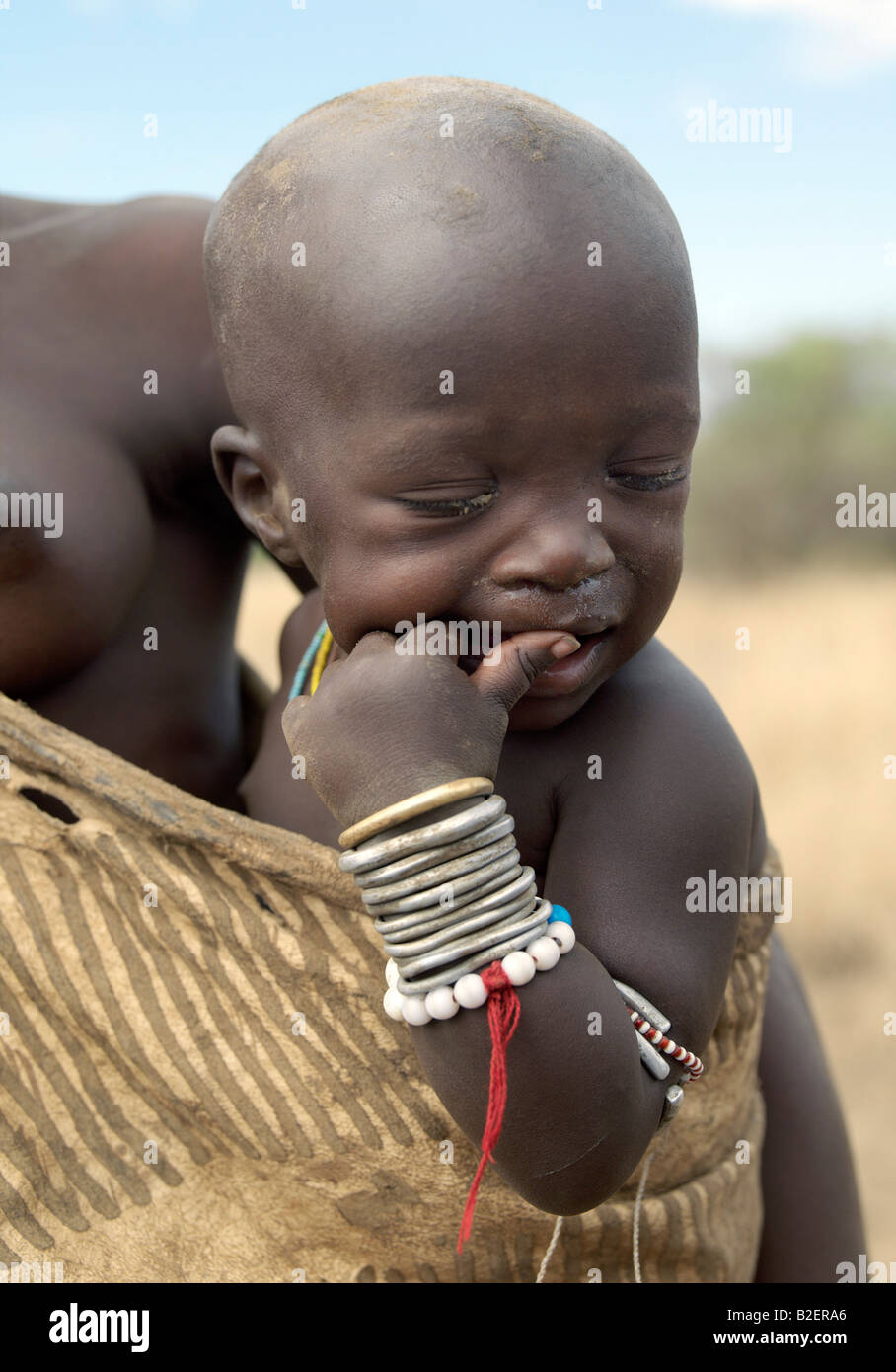 A Mursi child is carried safely in her mother's decorated leather ...