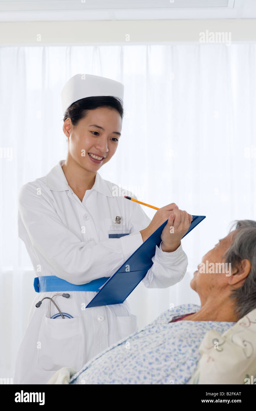 Female nurse writing on a medical chart with a patient lying in front ...