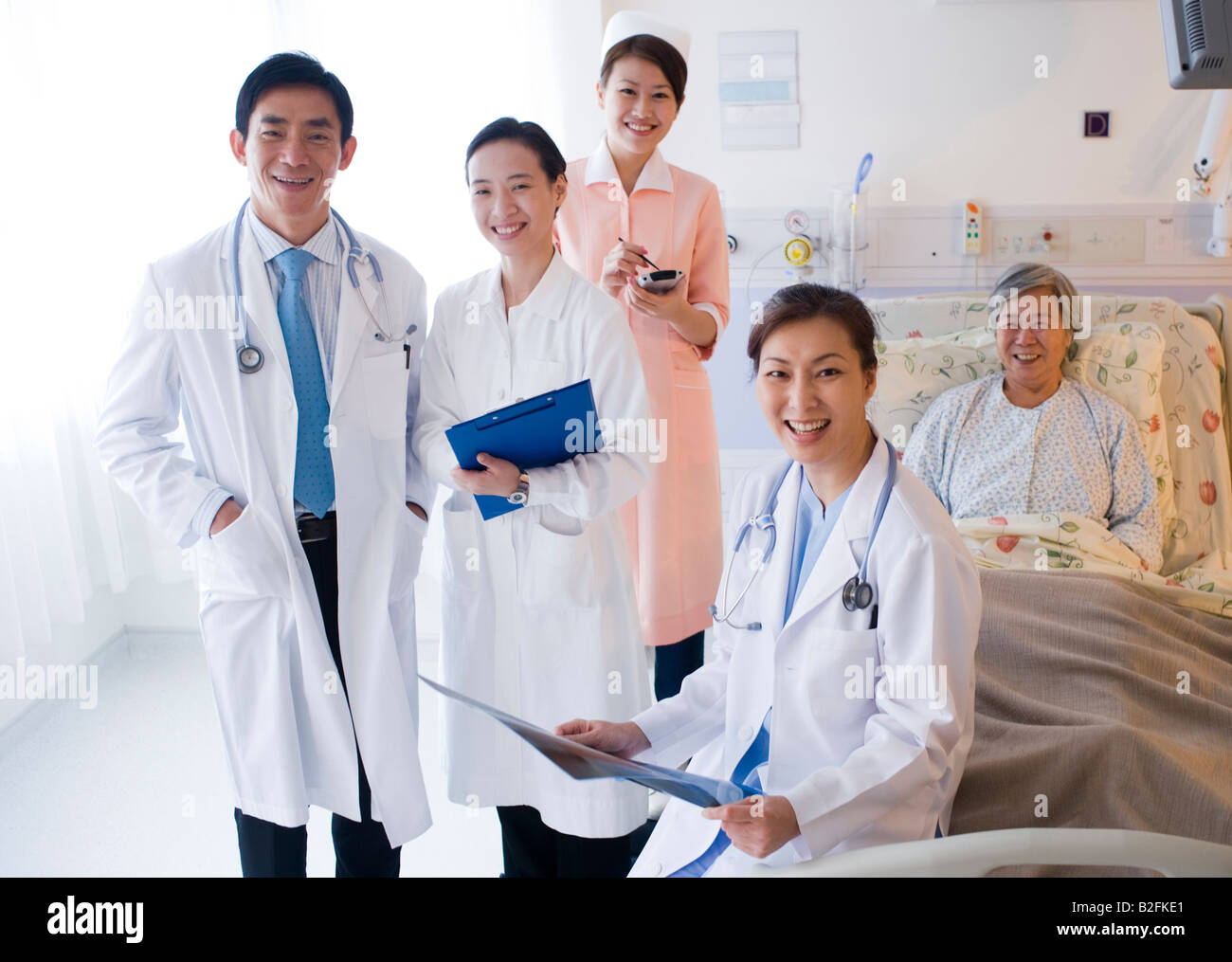 Two doctors and two female nurses with a patient in a hospital room ...