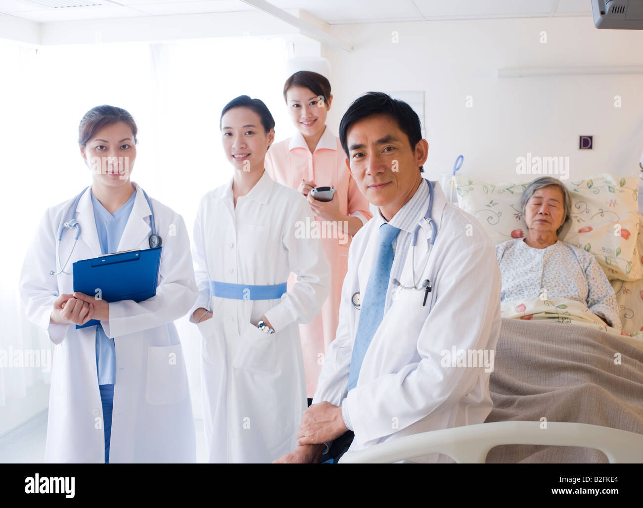 Two doctors and two female nurses with a patient in a hospital room ...