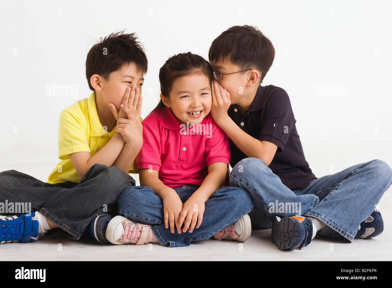 Two boys whispering into a girl's ears Stock Photo - Alamy