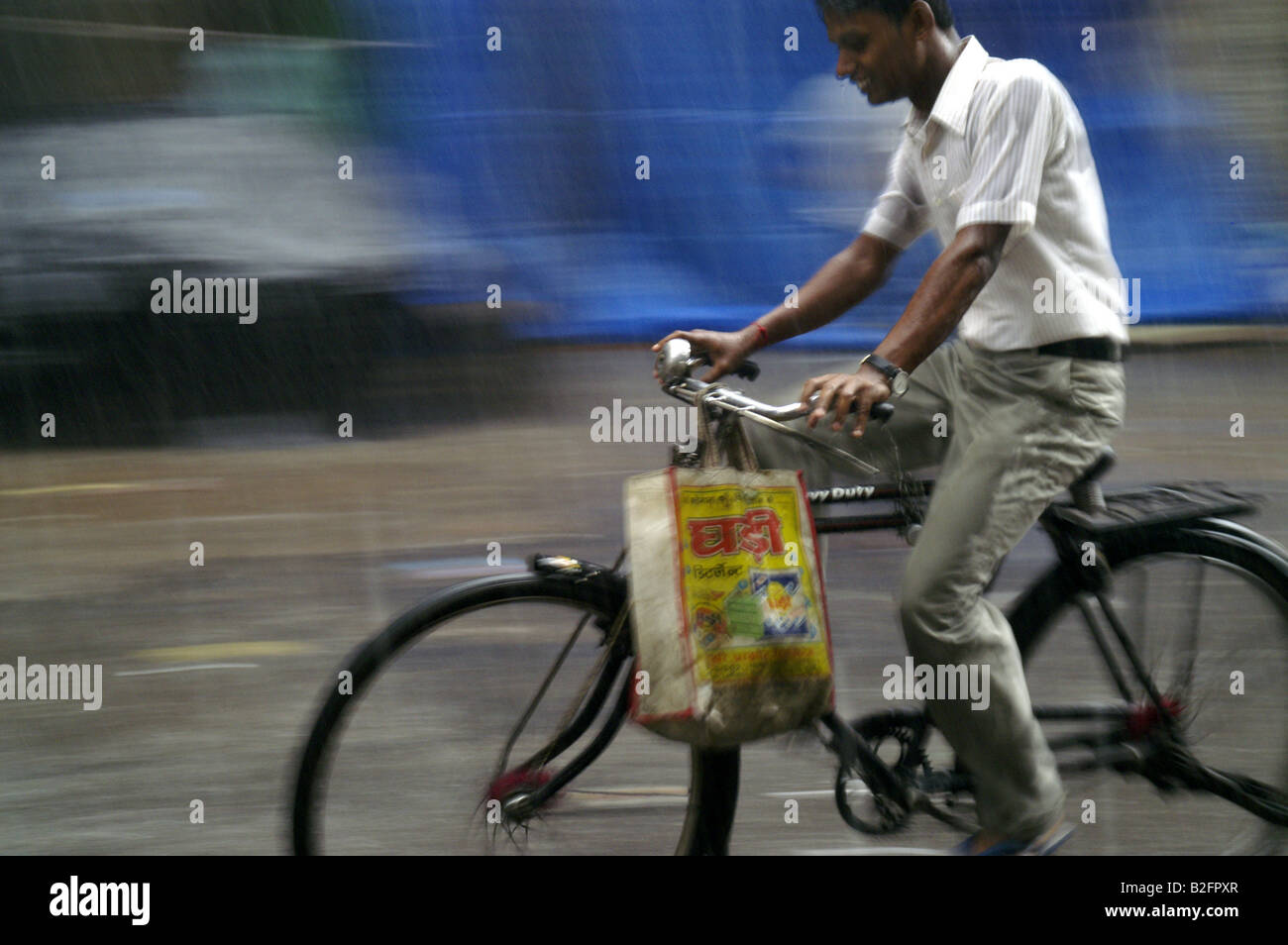 Indian man bicycle riding bike at street in Delhi in heavy monsoon rain ...