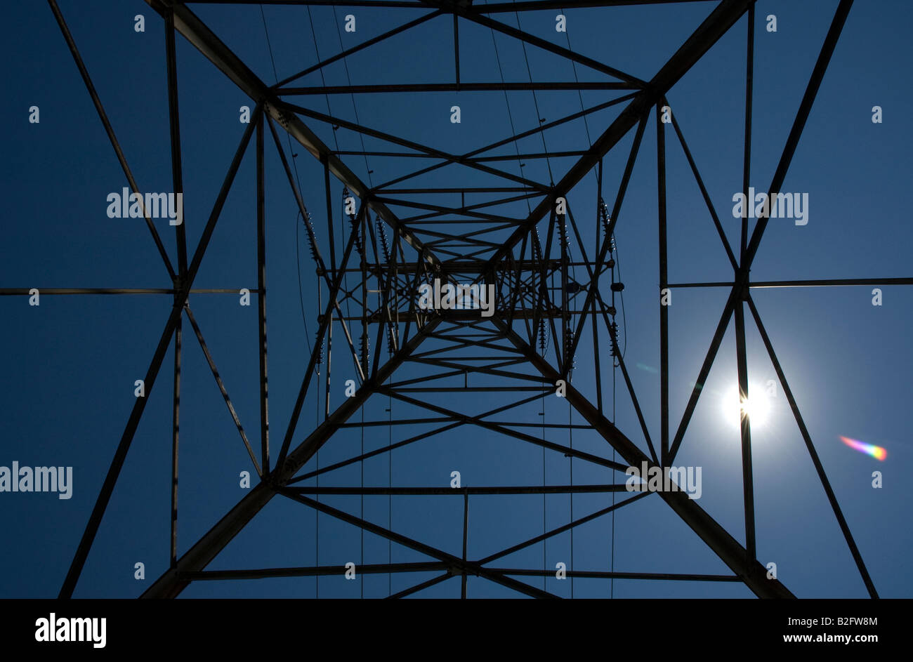 Electricity pylon (or tower) is back-lit by the sun over a blue sky ...