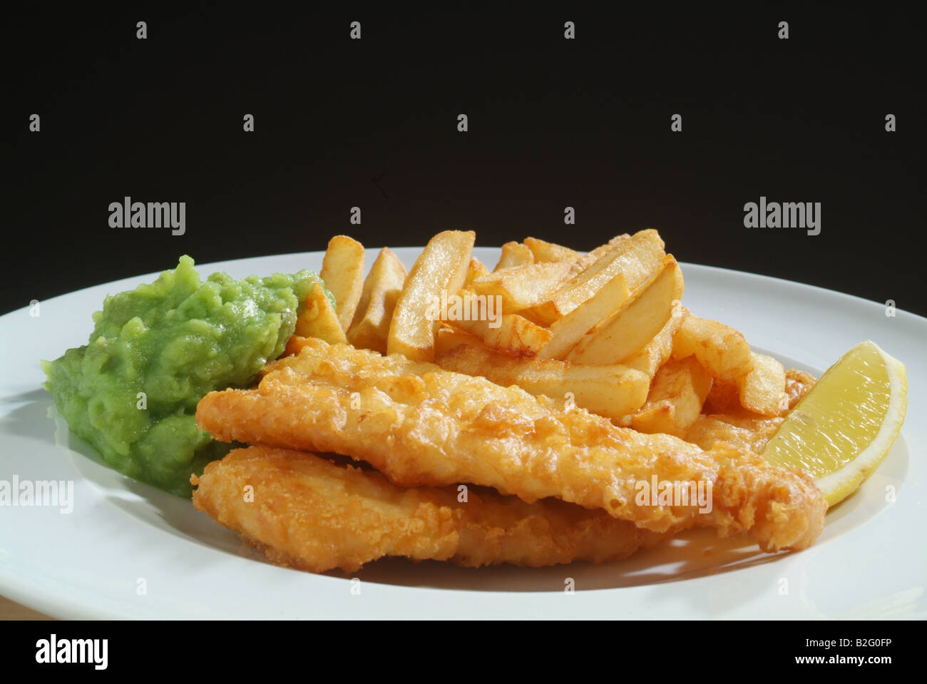 battered fish, chips,mushy peas and a slice of lemon, on a white plate ...