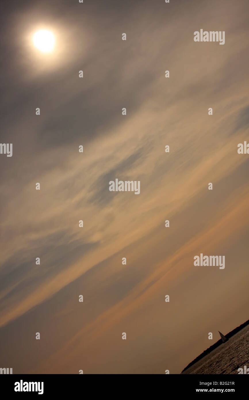 Sailing boat and falling sun behind some clouds Stock Photo - Alamy