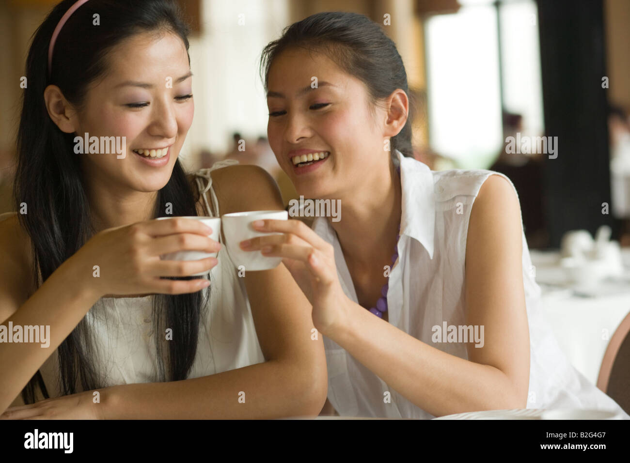 Two young women toasting with tea cups in a restaurant and smiling ...