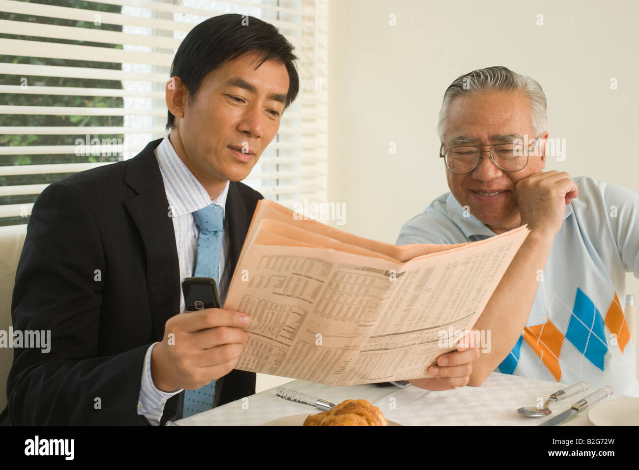 Mid adult man and his father reading a newspaper at a breakfast table ...