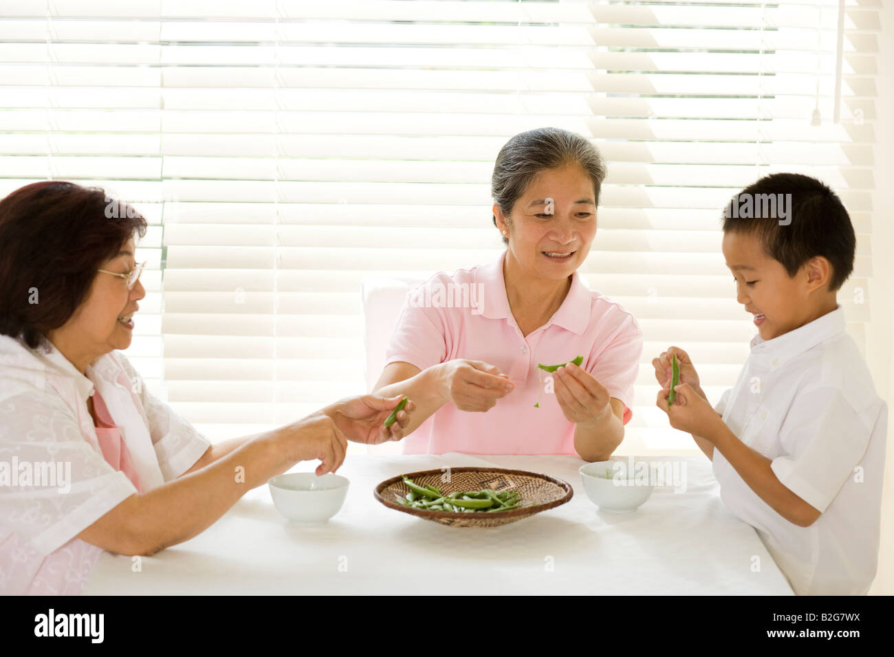 Two senior women with a boy shelling green peas at a dining table Stock ...