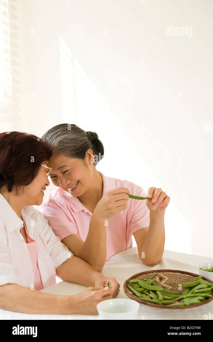 Two senior women peeling green peas and smiling Stock Photo - Alamy