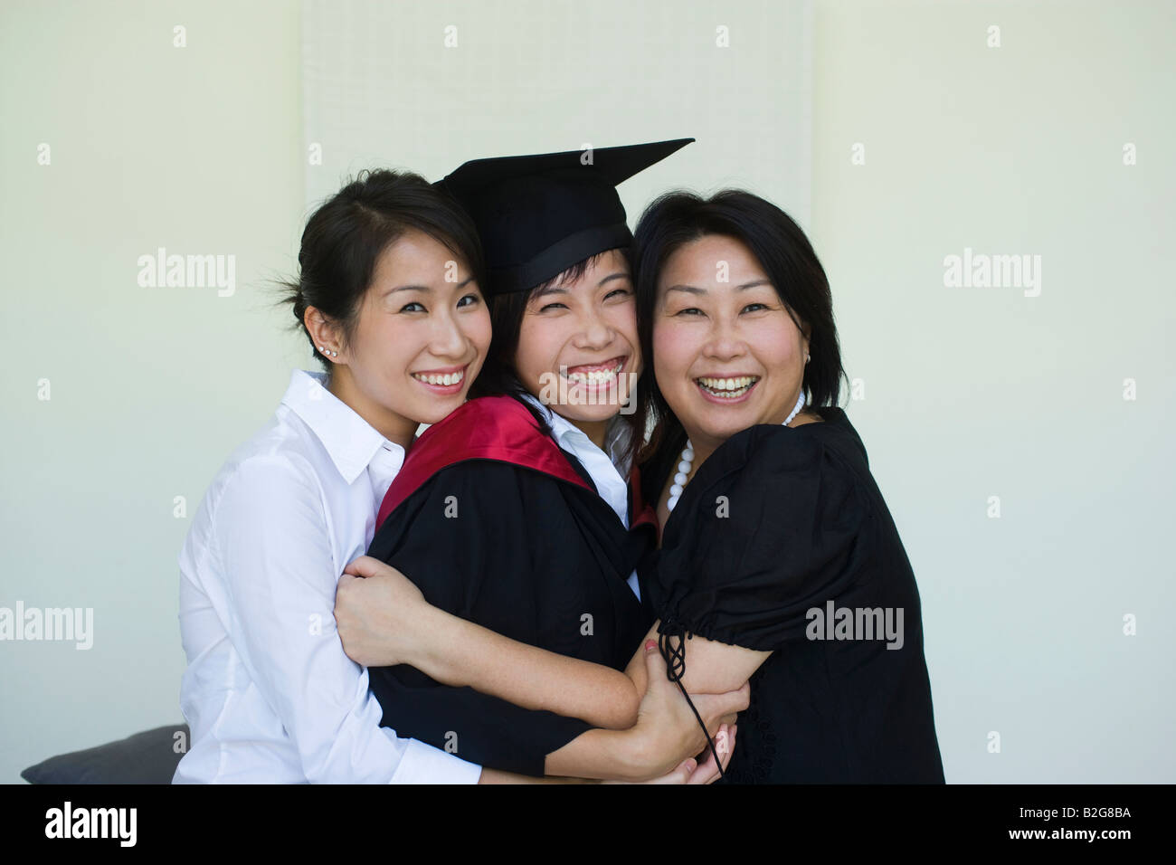 Portrait of a mid adult female graduate hugging her sisters and smiling ...