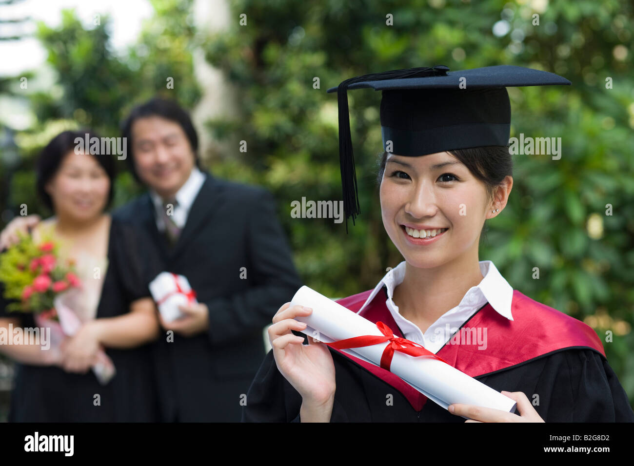 Portrait of a female graduate holding a diploma with her parents in the ...