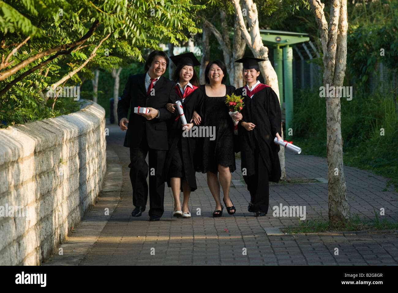 Portrait of two female graduates walking with their parents and smiling ...