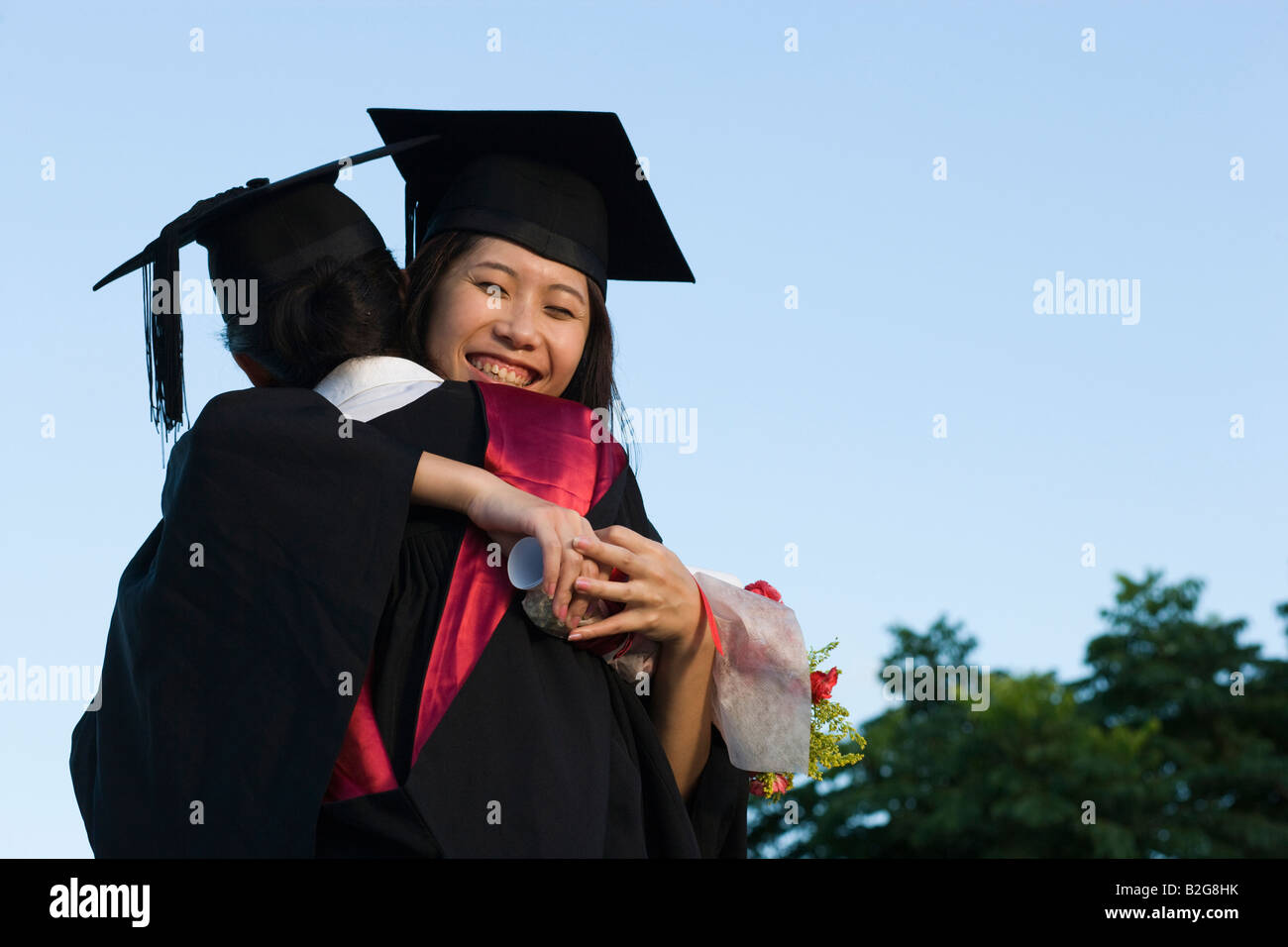 Low angle view of two female graduates hugging each other and smiling ...