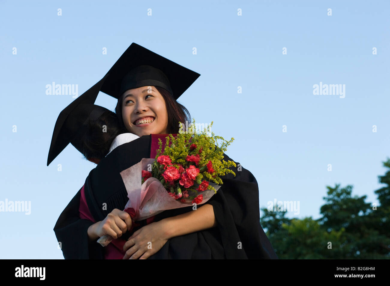 Low angle view of two female graduates hugging each other and smiling ...