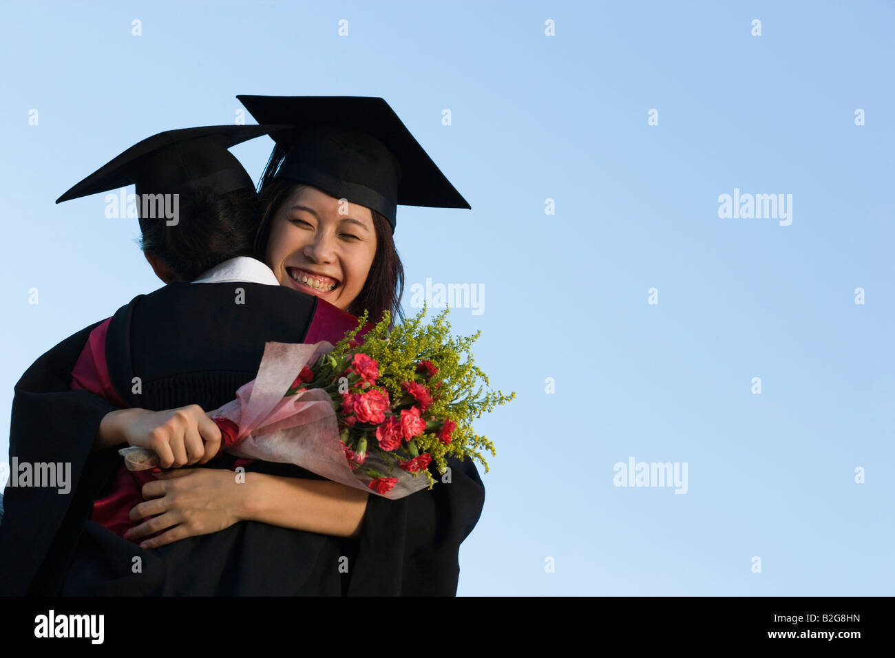 Low angle view of two female graduates hugging each other and smiling ...