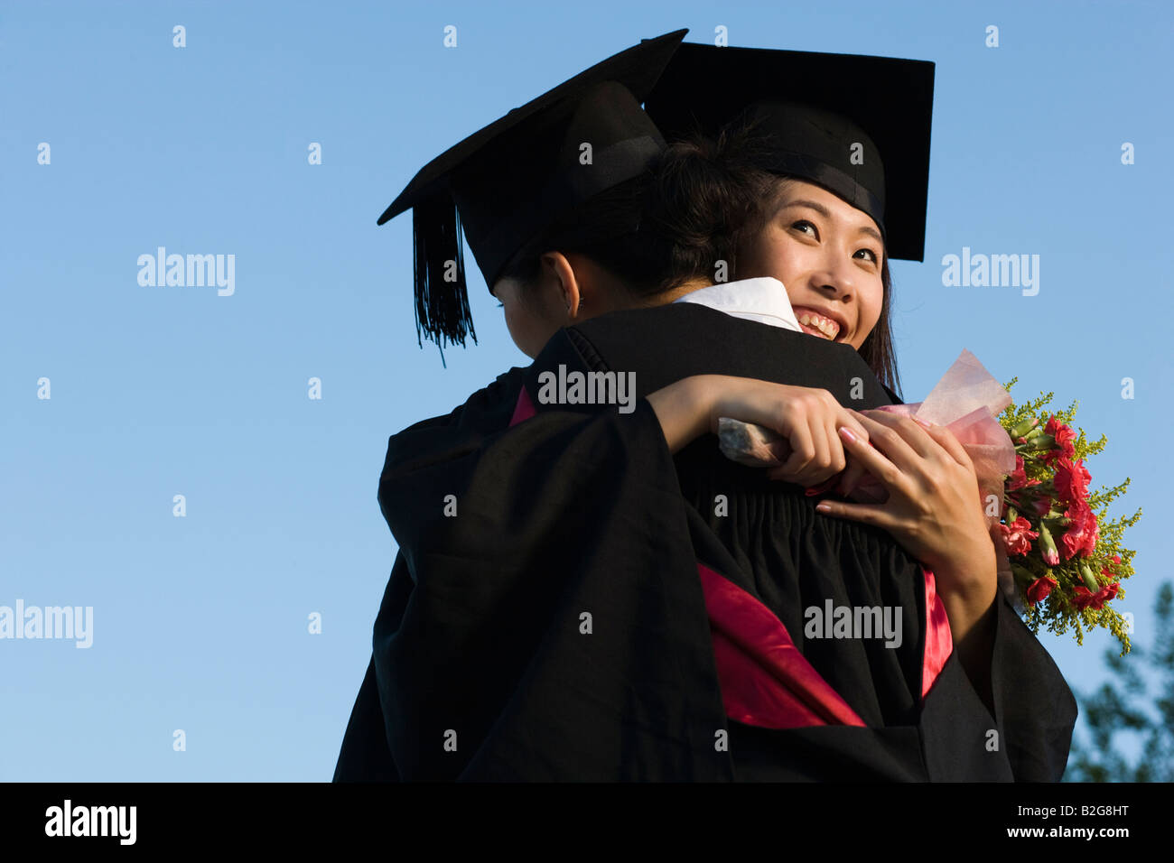 Low angle view of two female graduates hugging each other and smiling ...