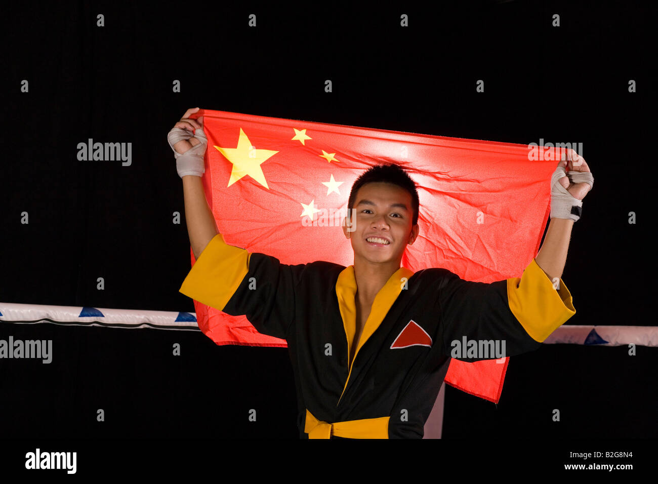 Portrait of a young man holding up a Chinese flag in a boxing ring ...