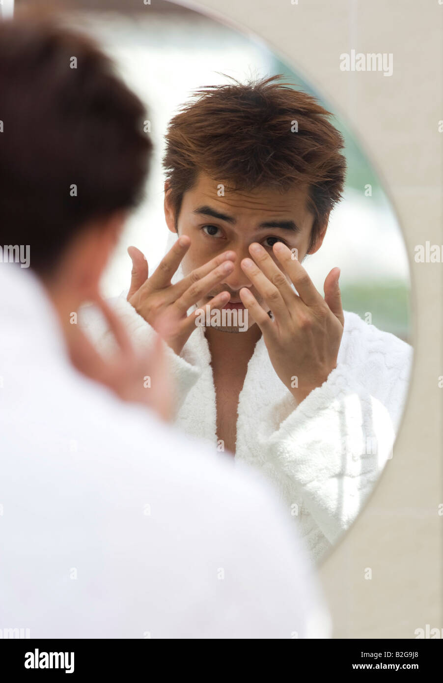 Young man examining his face in a mirror Stock Photo - Alamy