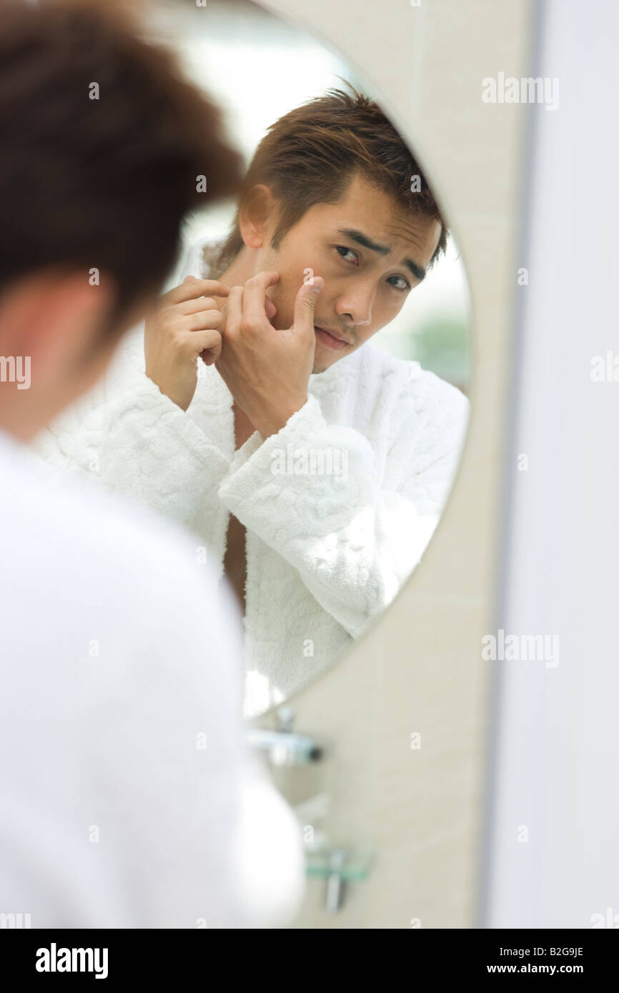 Young man examining his face in a mirror Stock Photo - Alamy