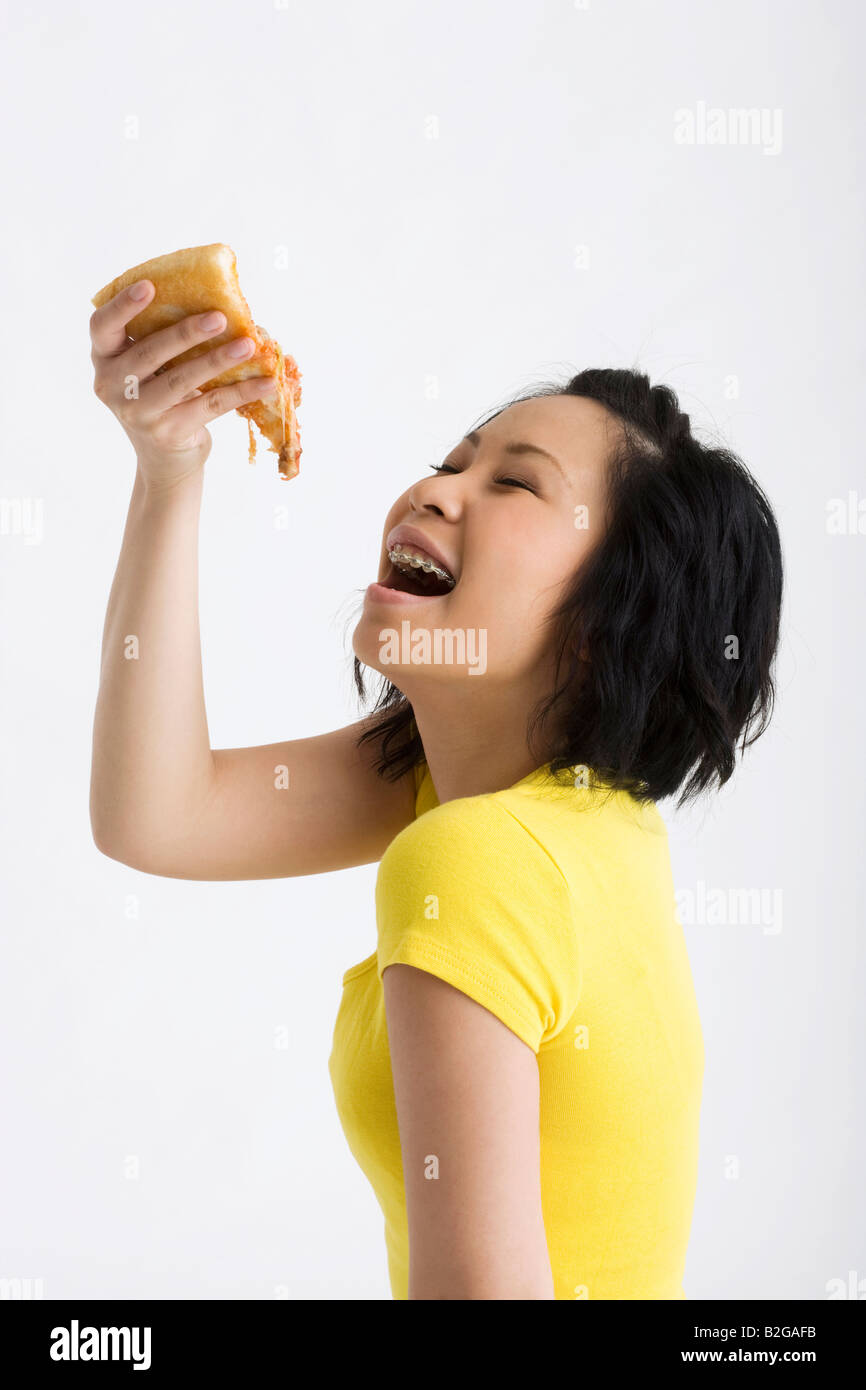 Side profile of a young woman eating a slice of pizza and laughing ...