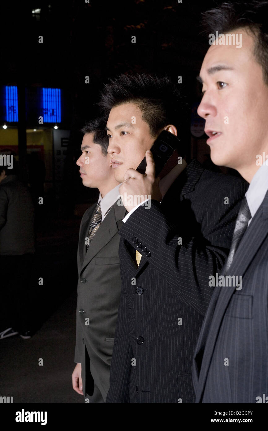 Side profile of a businessman talking on a mobile phone with another ...