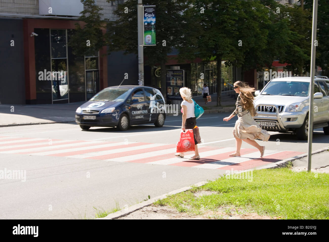 Two women crossing a street at a pedestrian crosswalk in Kyiv, carrying ...