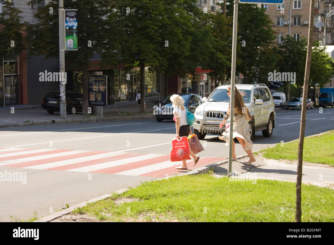 Two women crossing a street at a pedestrian crosswalk in Kyiv, carrying ...