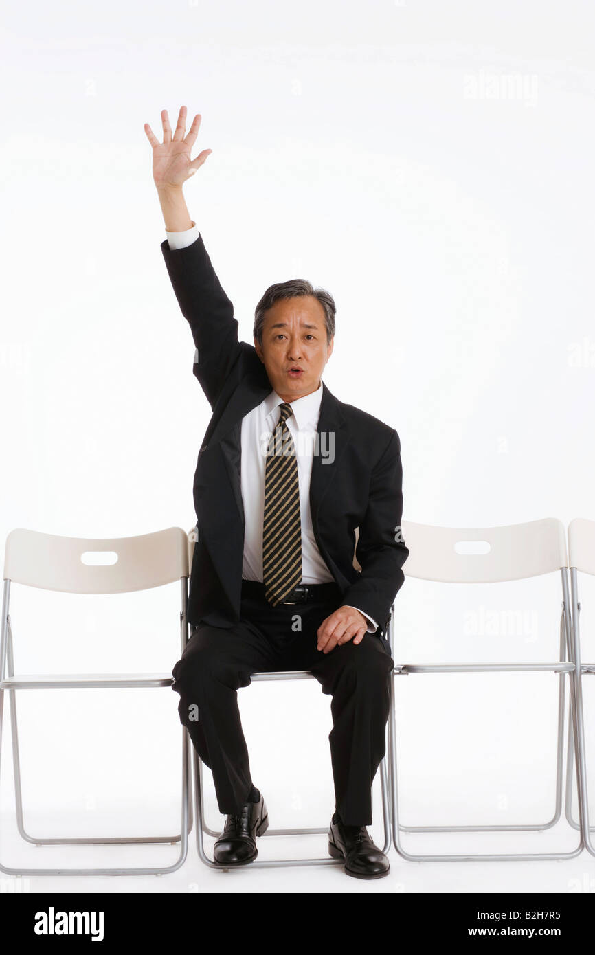 Portrait of a businessman sitting on a chair with his hand raised Stock ...