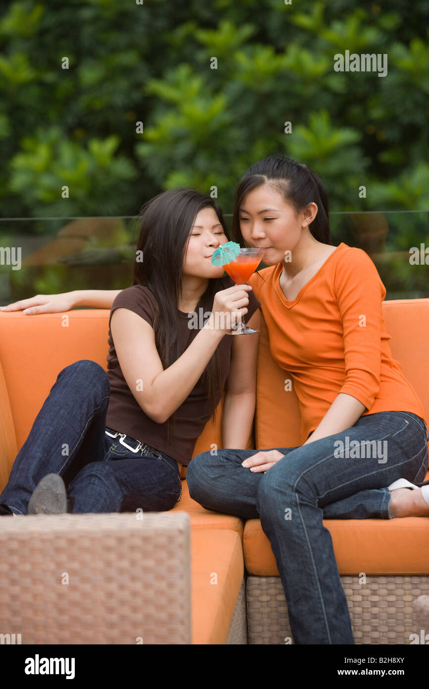 Two young women sitting on a couch and drinking a glass of cocktail ...