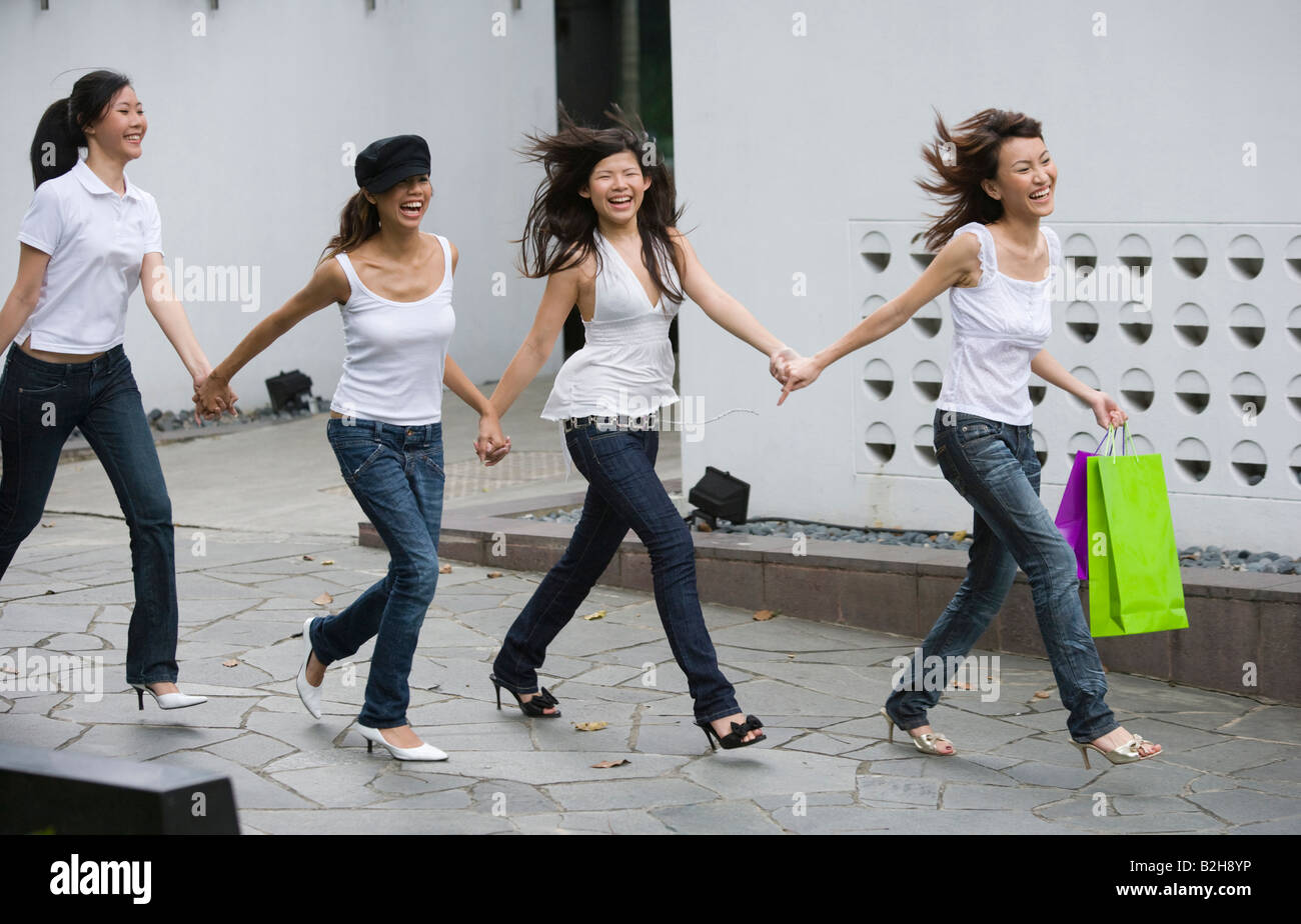 Four young women holding hands of each other and walking in a street ...