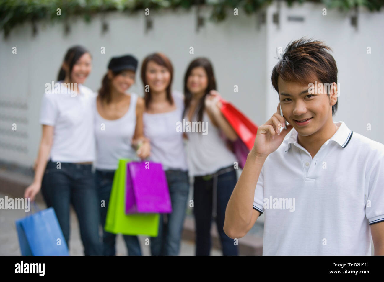 Portrait of a young man talking on a mobile phone with four young women ...