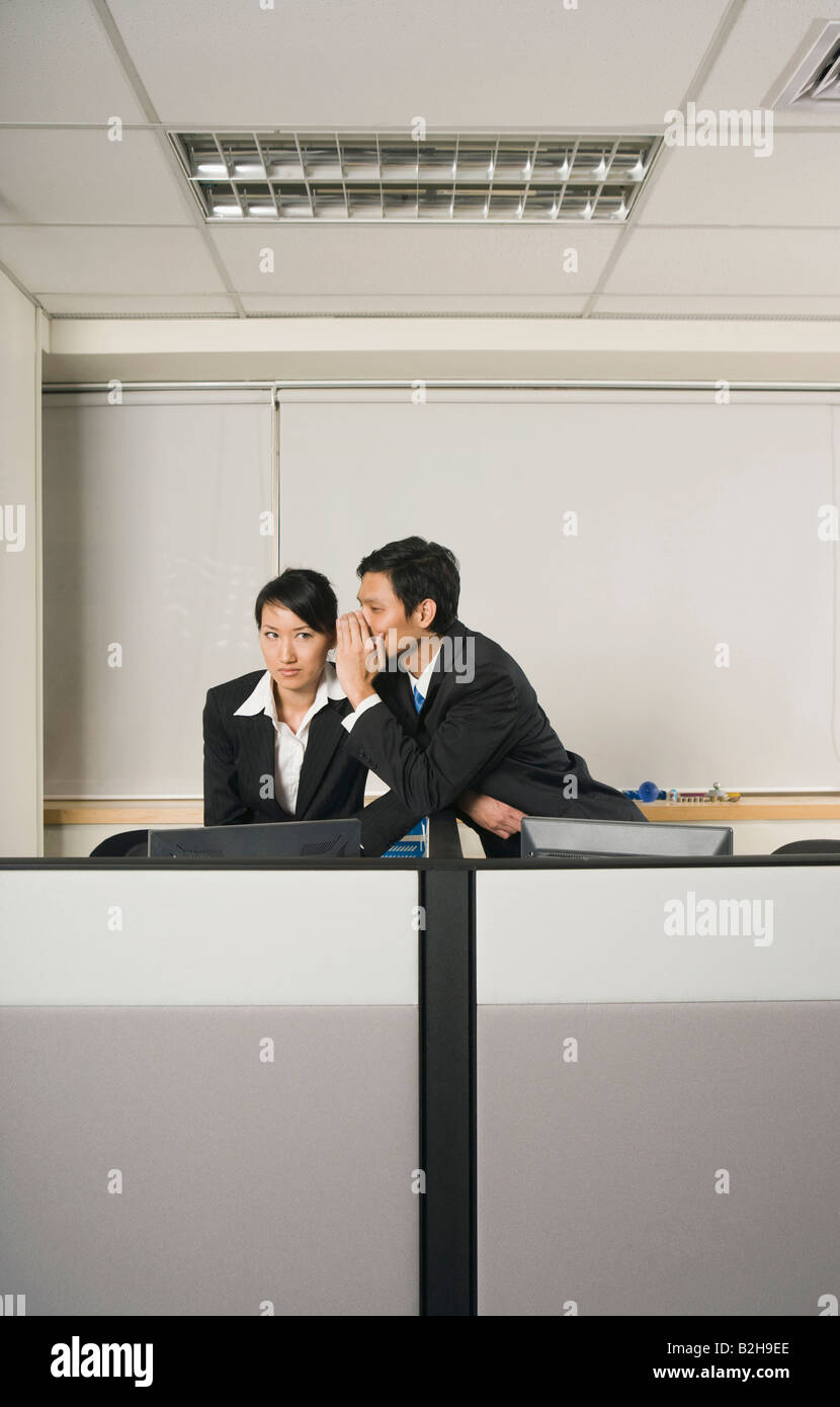 Businessman whispering into a businesswoman's ear from office cubicle ...