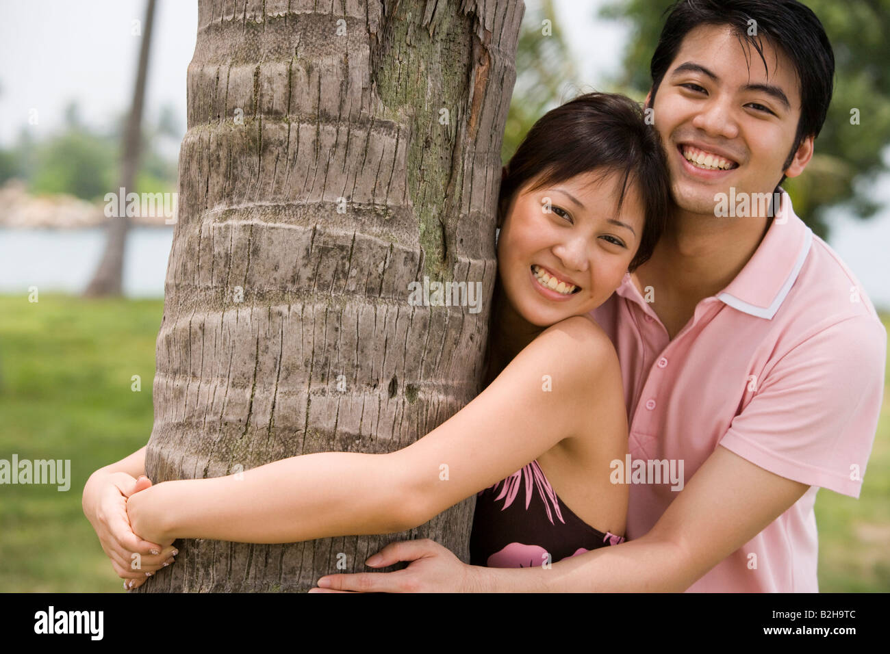 Portrait of a young couple hugging a tree trunk and smiling Stock Photo ...