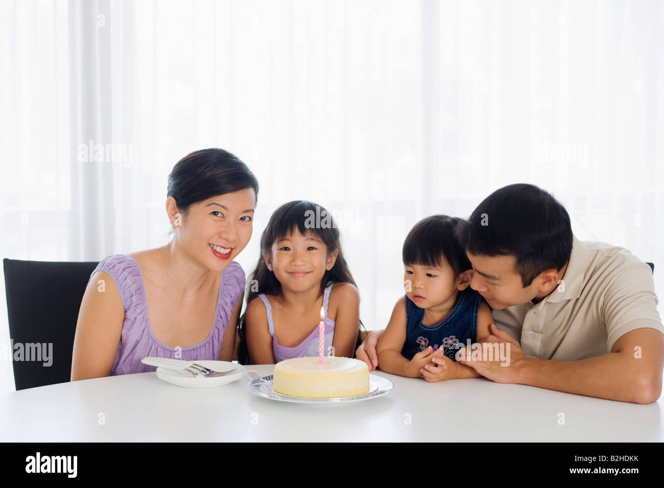 Mid adult couple sitting in front of a birthday cake with their two ...
