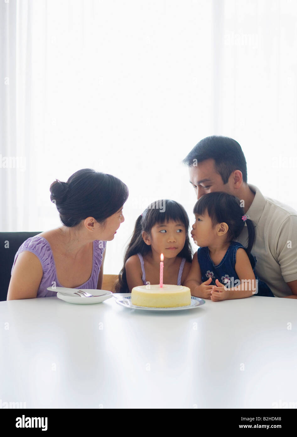 Mid adult couple sitting in front of a birthday cake with their two ...
